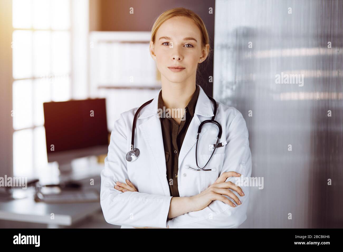 Cheerful smiling female doctor standing with arms crossed in clinic ...