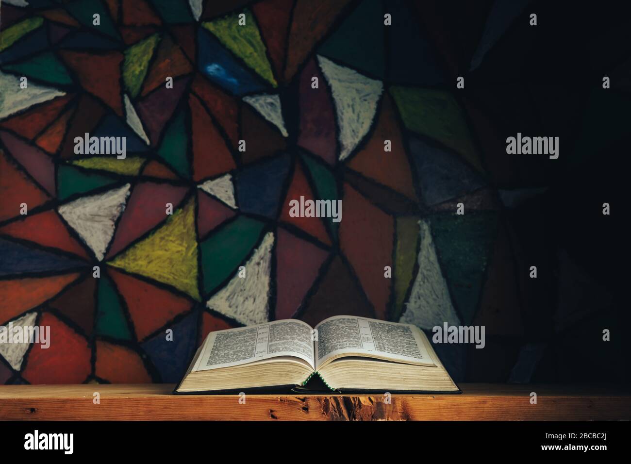 Open Holy Bible on a red wooden table. Beautiful Stained-glass windows ...