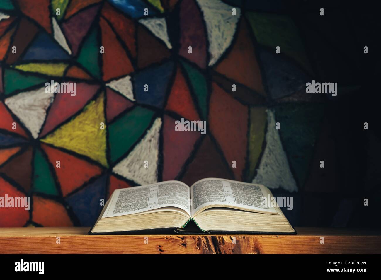 Open Holy Bible on a red wooden table. Beautiful Stained-glass windows ...