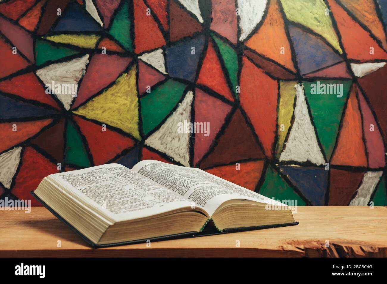 Close up open Holy Bible on a red wooden table. Beautiful Stained-glass ...