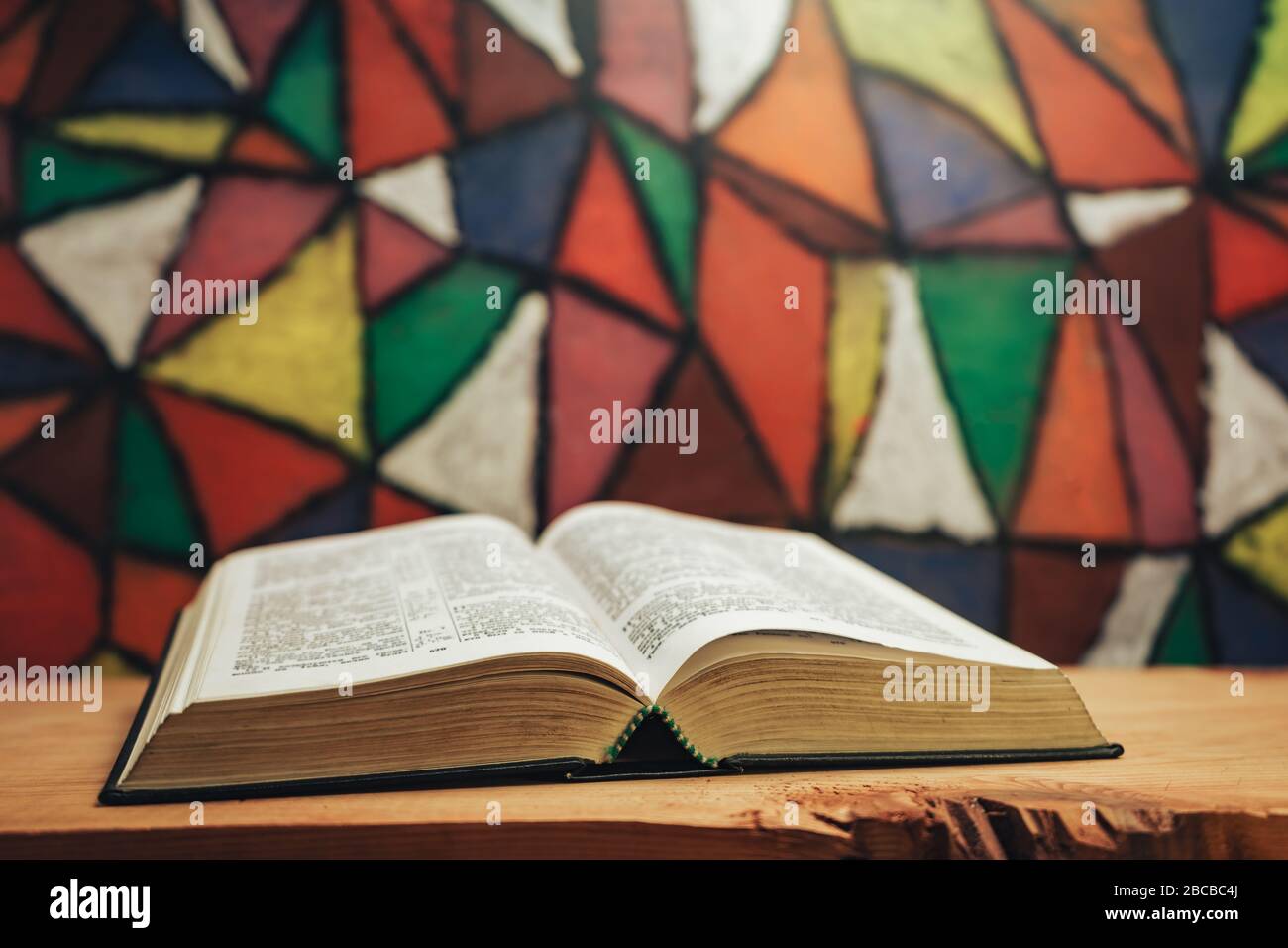 Close up open Holy Bible on a red wooden table. Beautiful Stained-glass ...