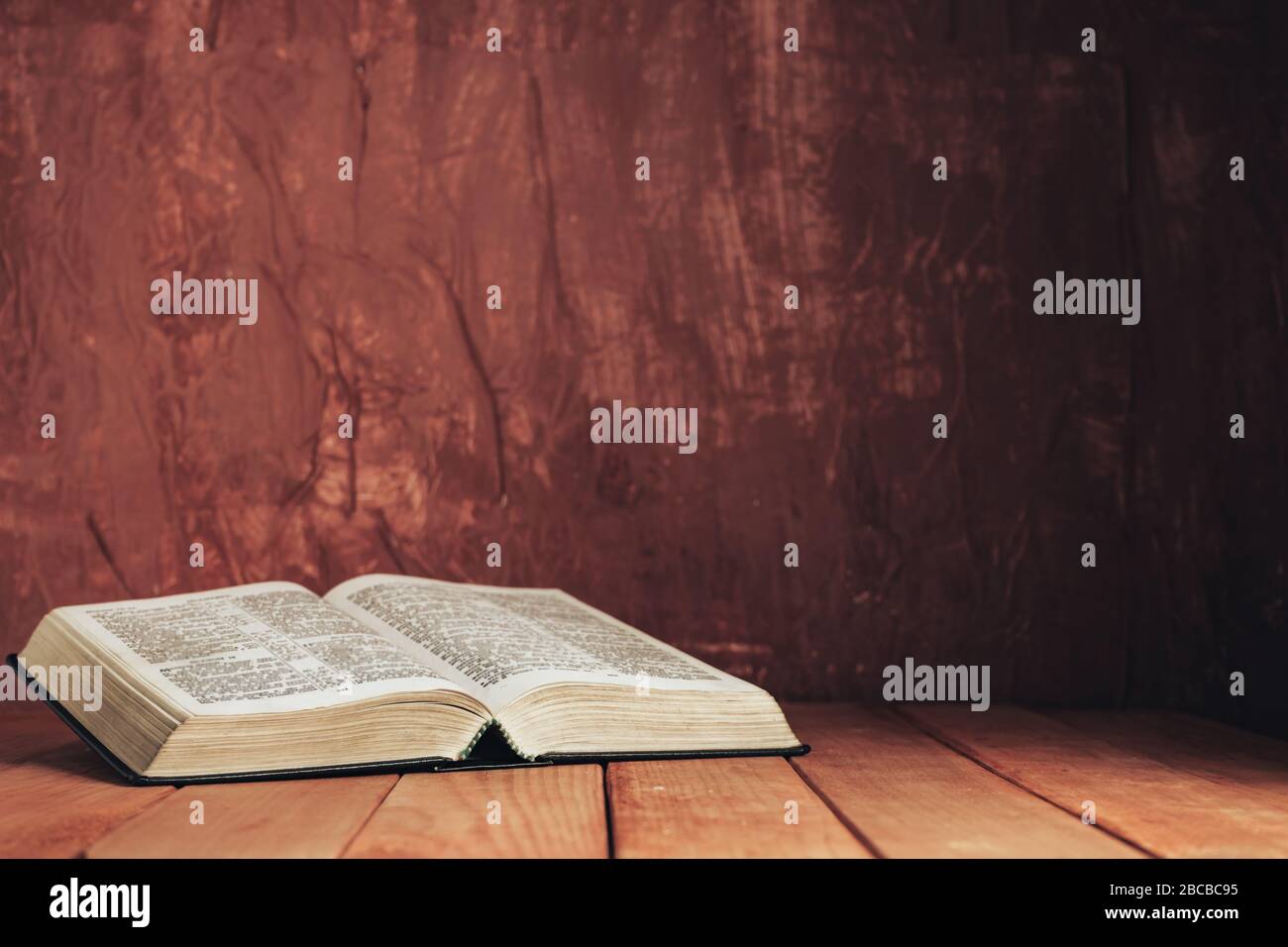 Open bible on a red old wooden table. Beautiful brown wall background ...