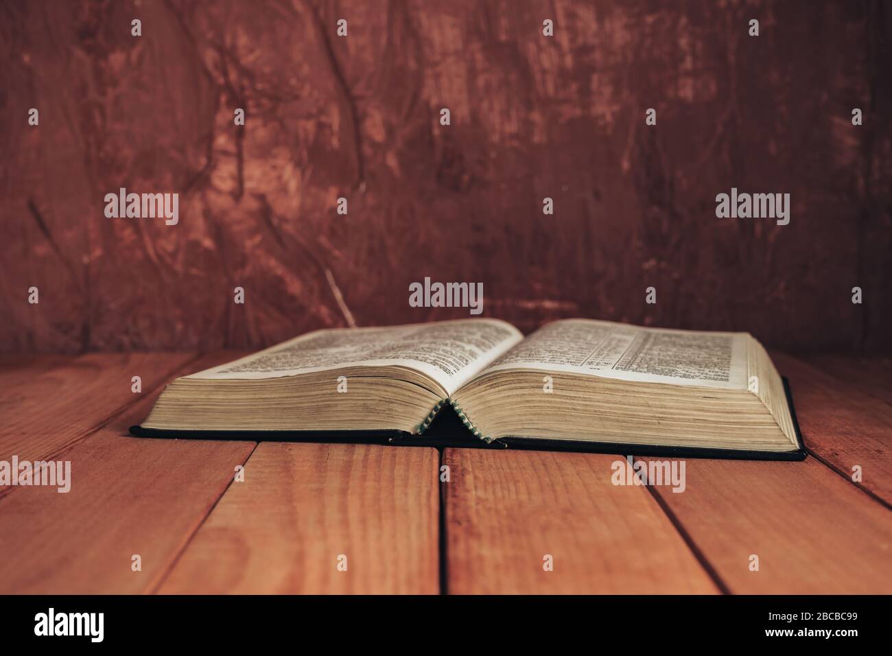 Open bible on a red old wooden table. Beautiful brown wall background ...