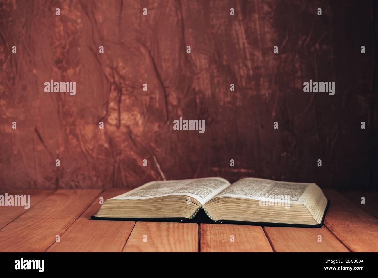 Open bible on a red old wooden table. Beautiful brown wall background ...