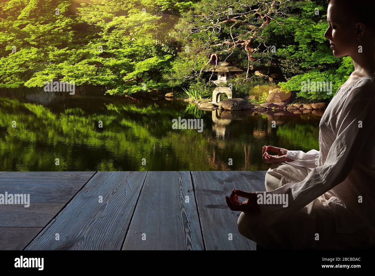 Beautiful young woman in white robe sits in meditation in Zen garden on ...