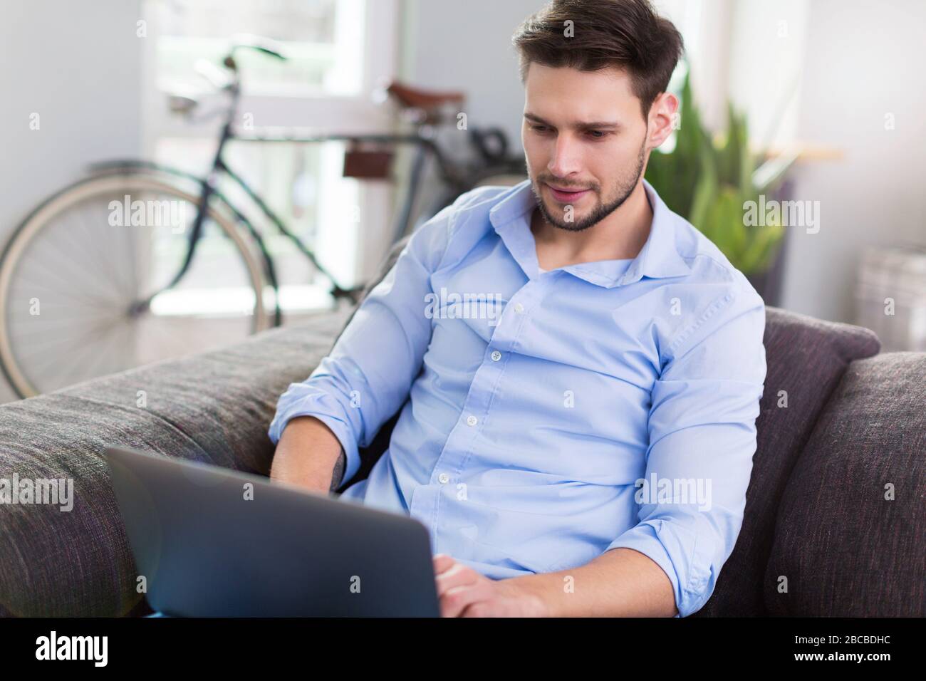 Man sitting on couch with laptop Stock Photo - Alamy