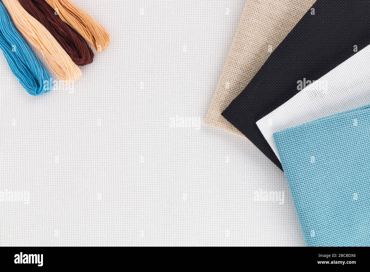 Different color of thread for sewing and canvas for embroidery lying on ...