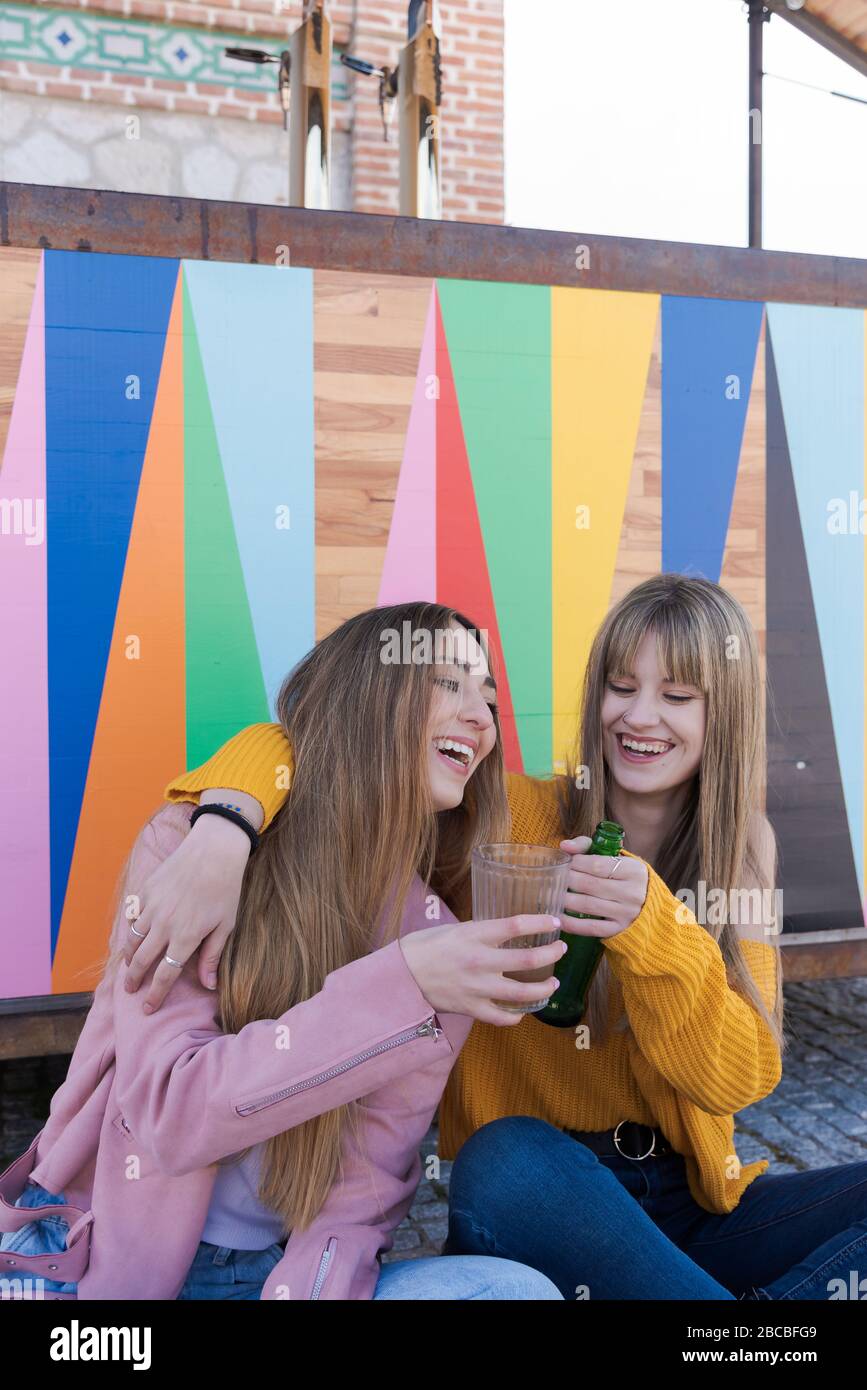 Two happy young Caucasian women toast with drink on the multicolored ...