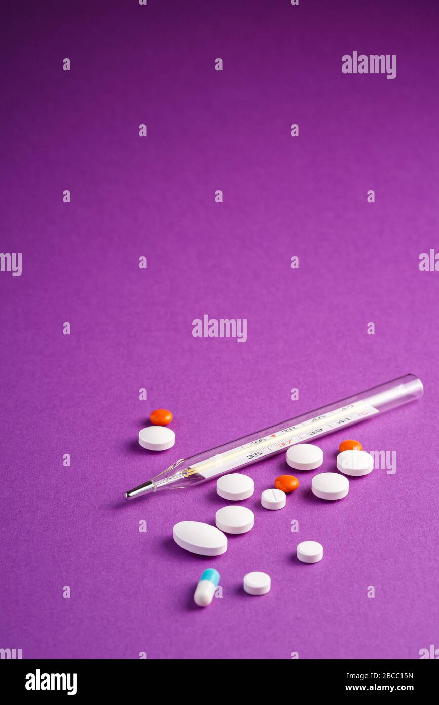 Pills, tablets and analog thermometer on violet purple background ...