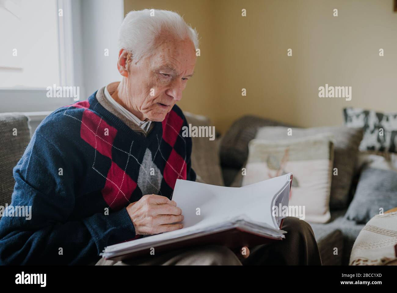 Old man reading book sitting on couch Stock Photo - Alamy
