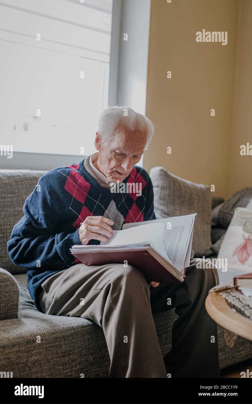 Old man reading book sitting on couch Stock Photo - Alamy