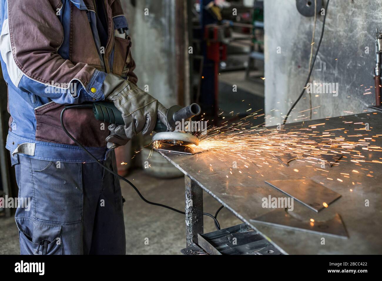 Workman with a mask and gloves is grinding a metal object with a ...