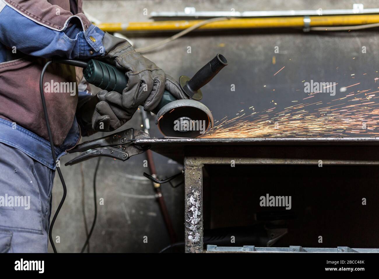 Workman with a mask and gloves is grinding a metal object with a ...