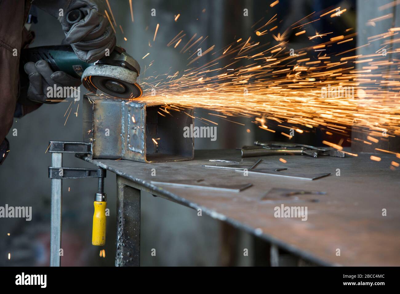 Workman with a mask and gloves is grinding a metal object with a ...