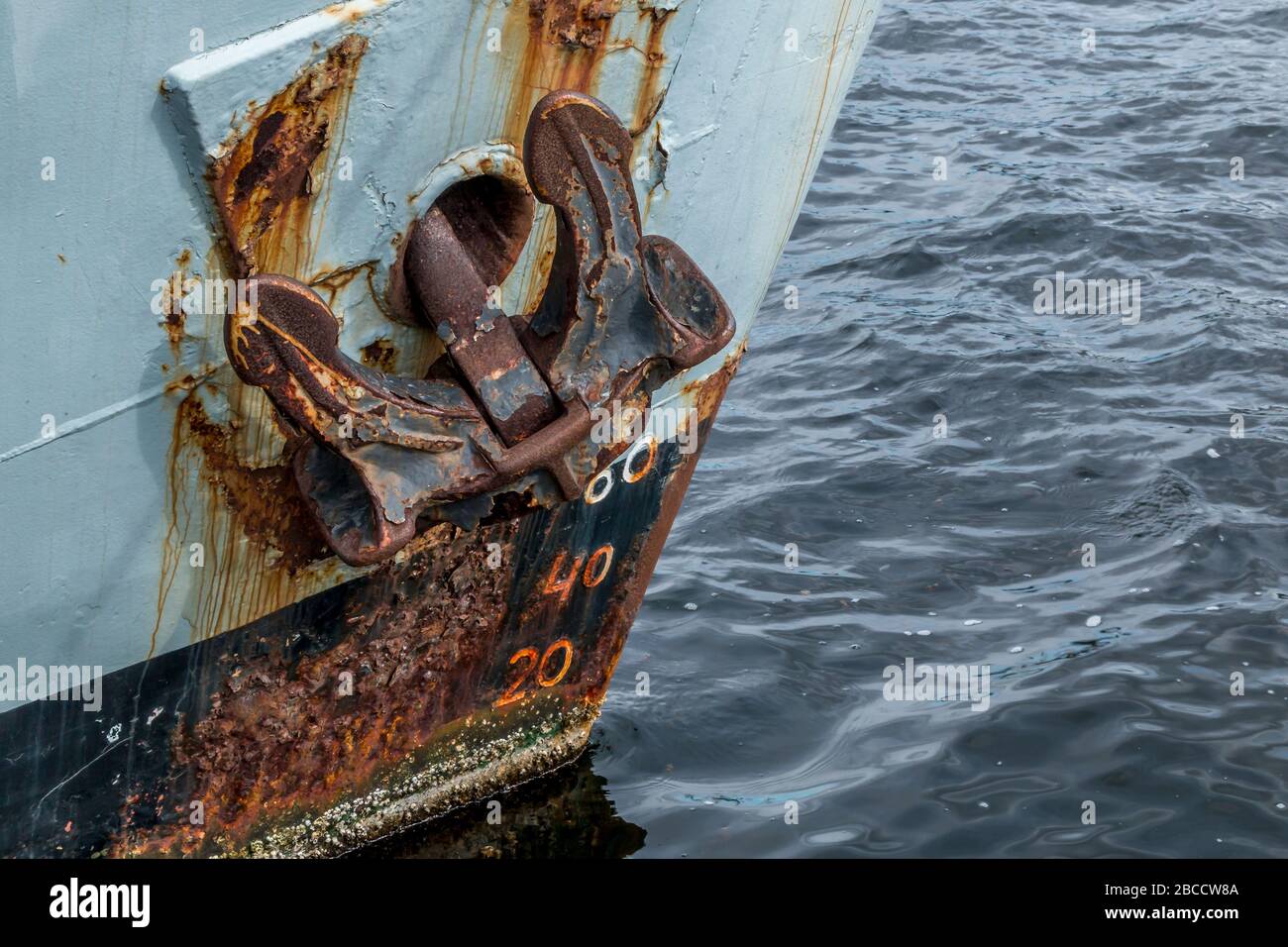 The rust anchor on the front of a gray steel ship. Ship is in the ...