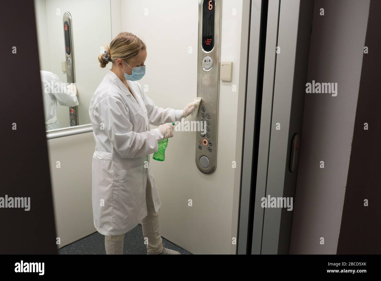 Woman using wet wipe and alcohol sanitizer spray to clean an elevator ...