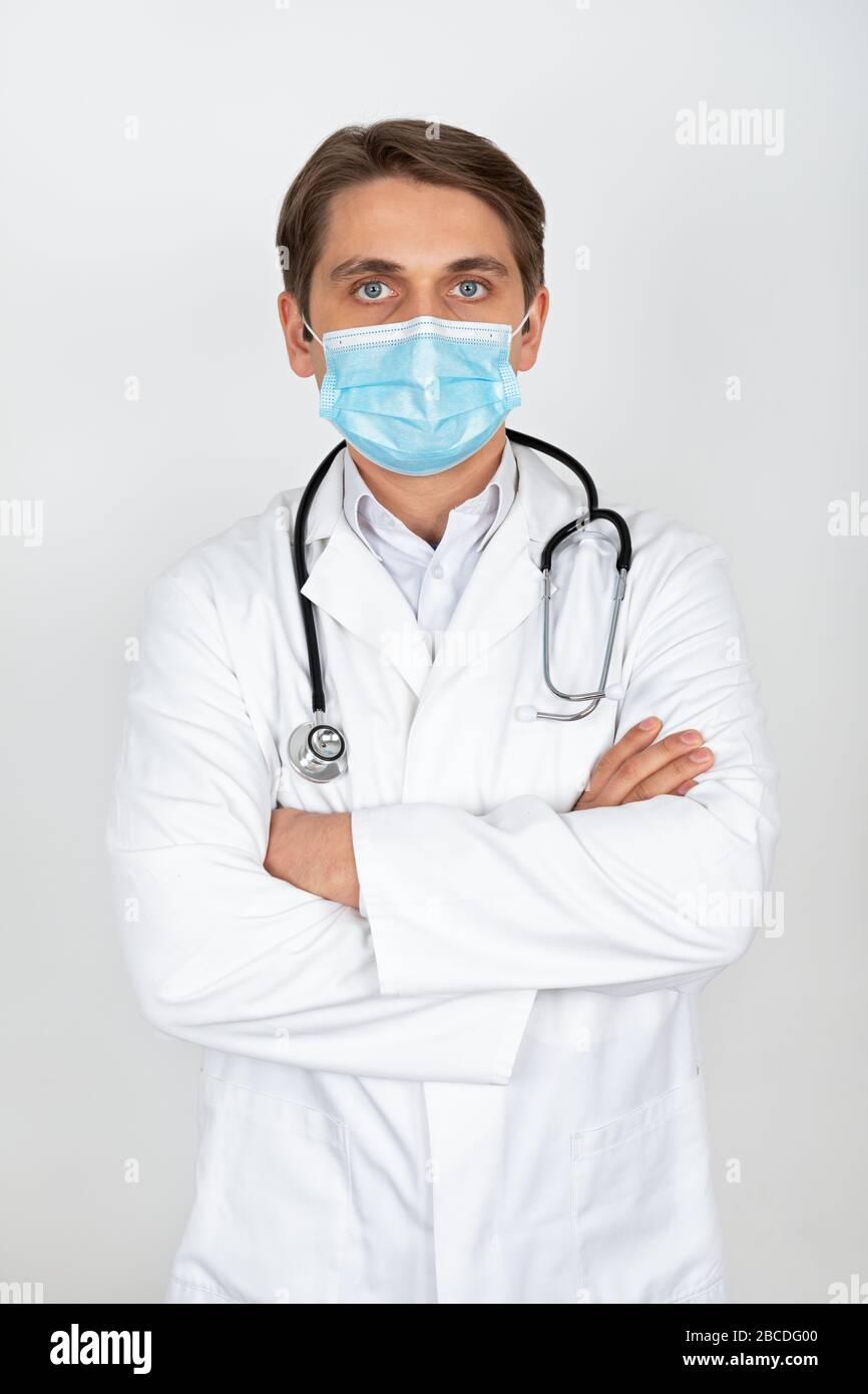 Handsome young physician wearing surgical mask is looking to the camera ...