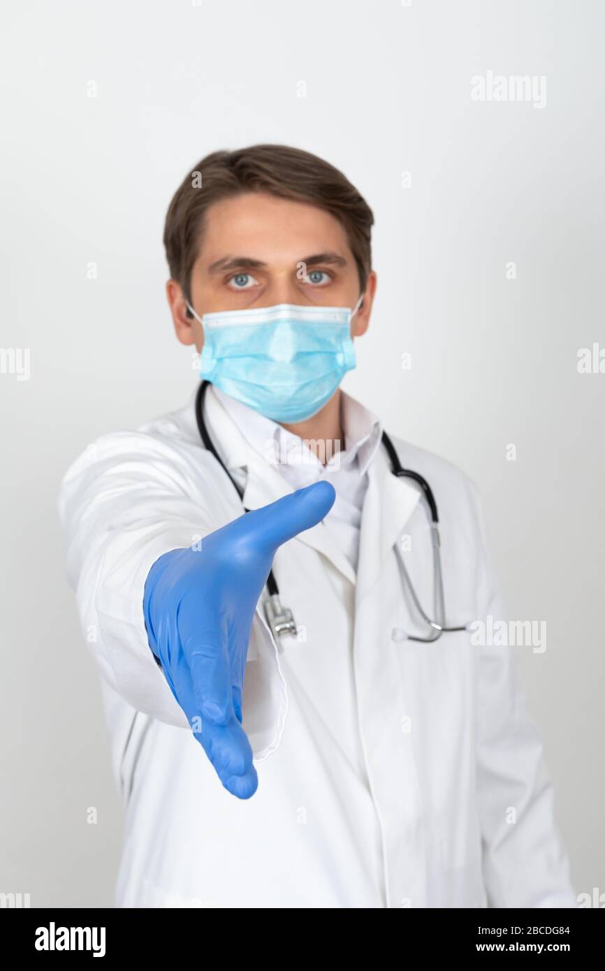 Handsome young physician wearing surgical mask is showing handshake on ...