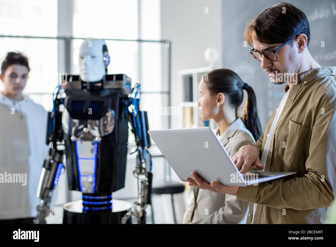Young serious teacher with laptop looking through online materials ...