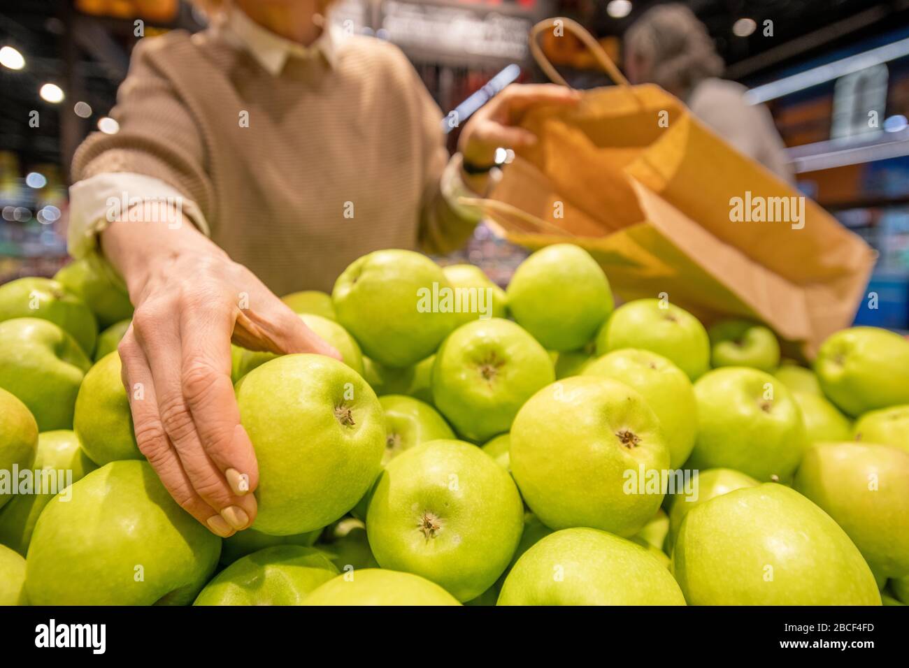 Hand of aged woman with paperbag taking fresh granny smith apple while ...