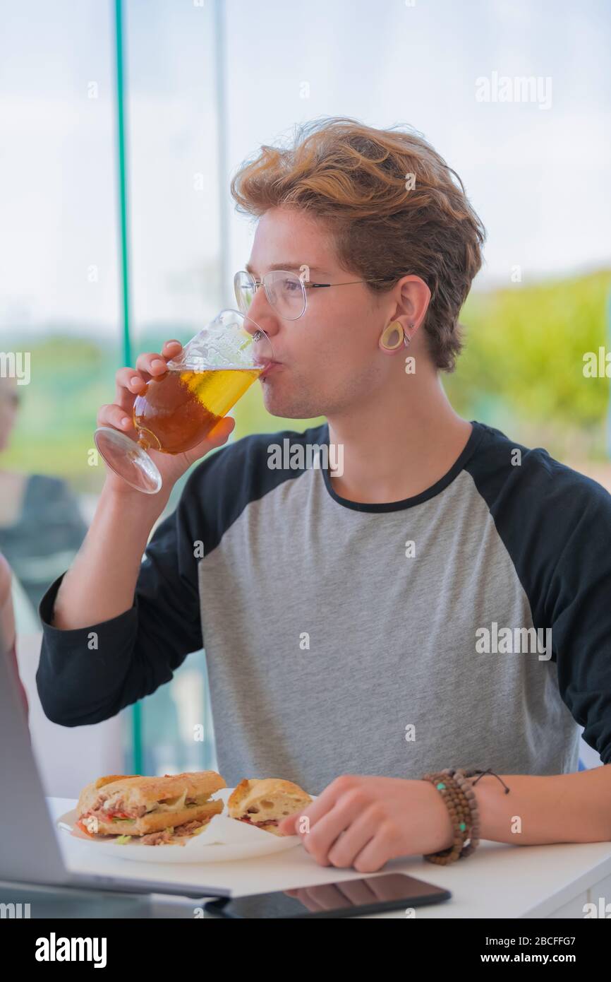 young man drinking beer sitting in front of a table in which there are ...
