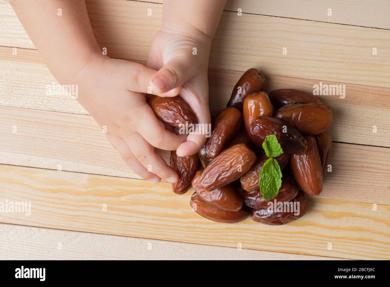 Kids hand holding dates on a wooden background, mint inside Stock Photo ...