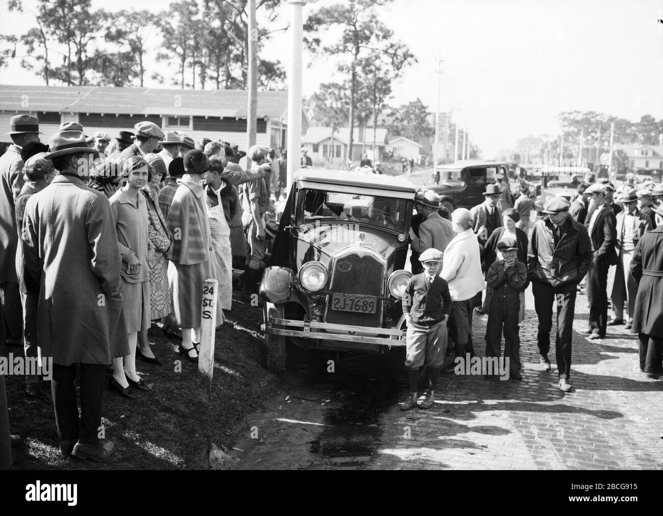 A group of onlookers gather around a car crashed alongside a road ...