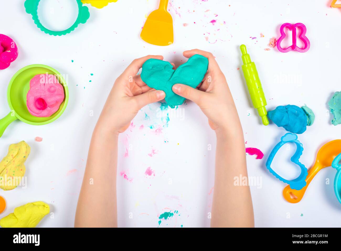 Little girl hands close up playing with colorful modeling clay on white ...