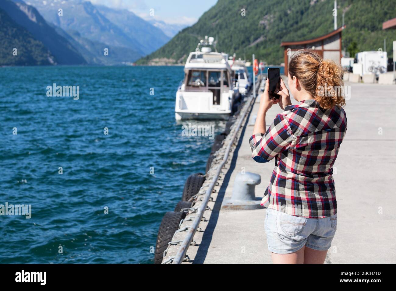 European woman shooting fjord with her smartphone standing on pier of ...