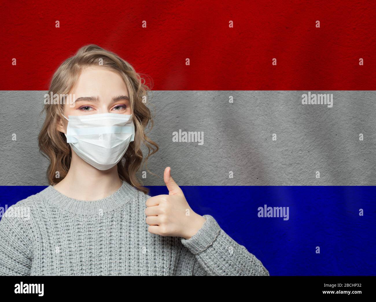 Happy woman in face mask holding thumb up on Netherlands flag ...