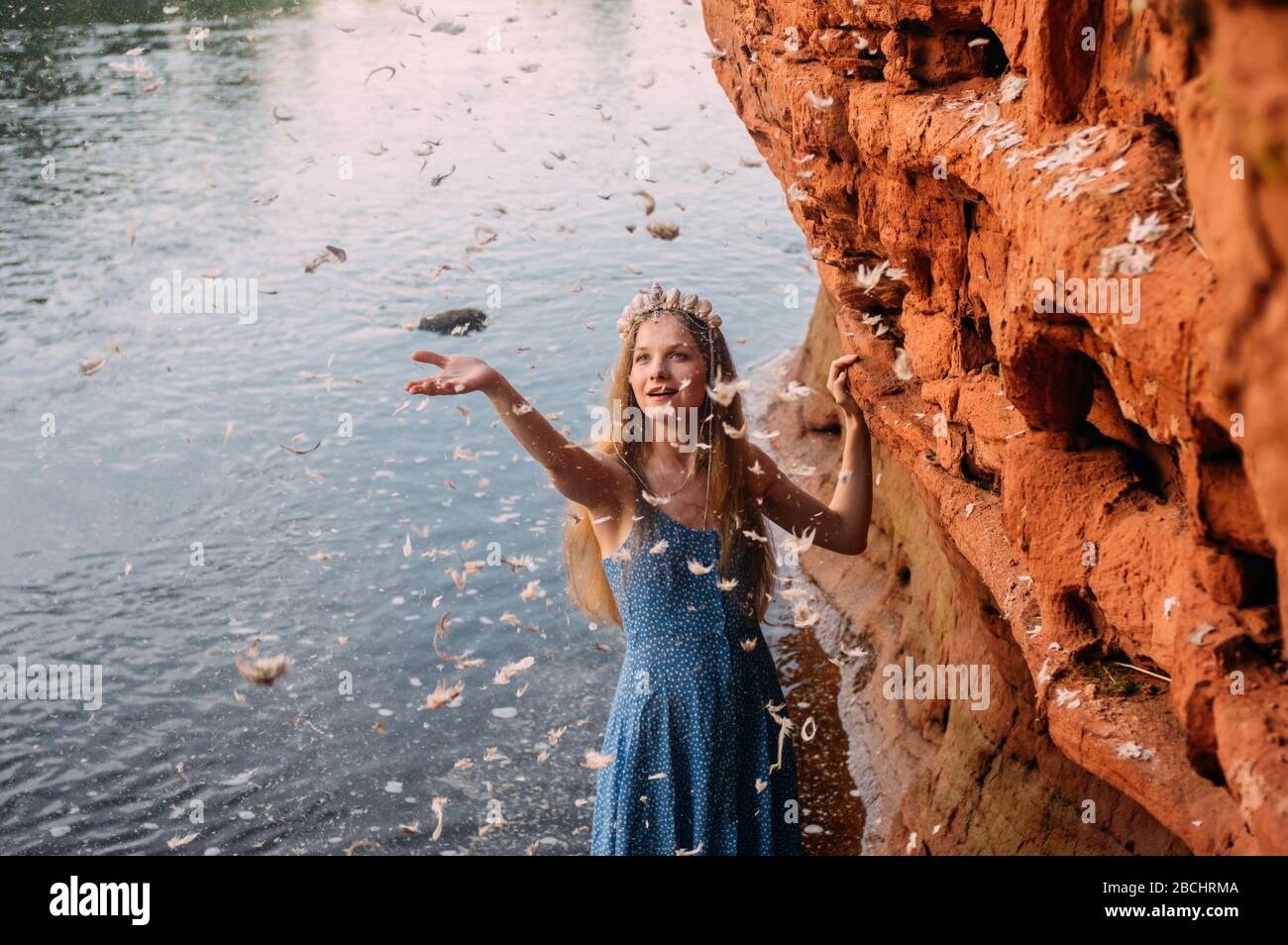 Young woman in crown from shells staying near red sand wall in river ...