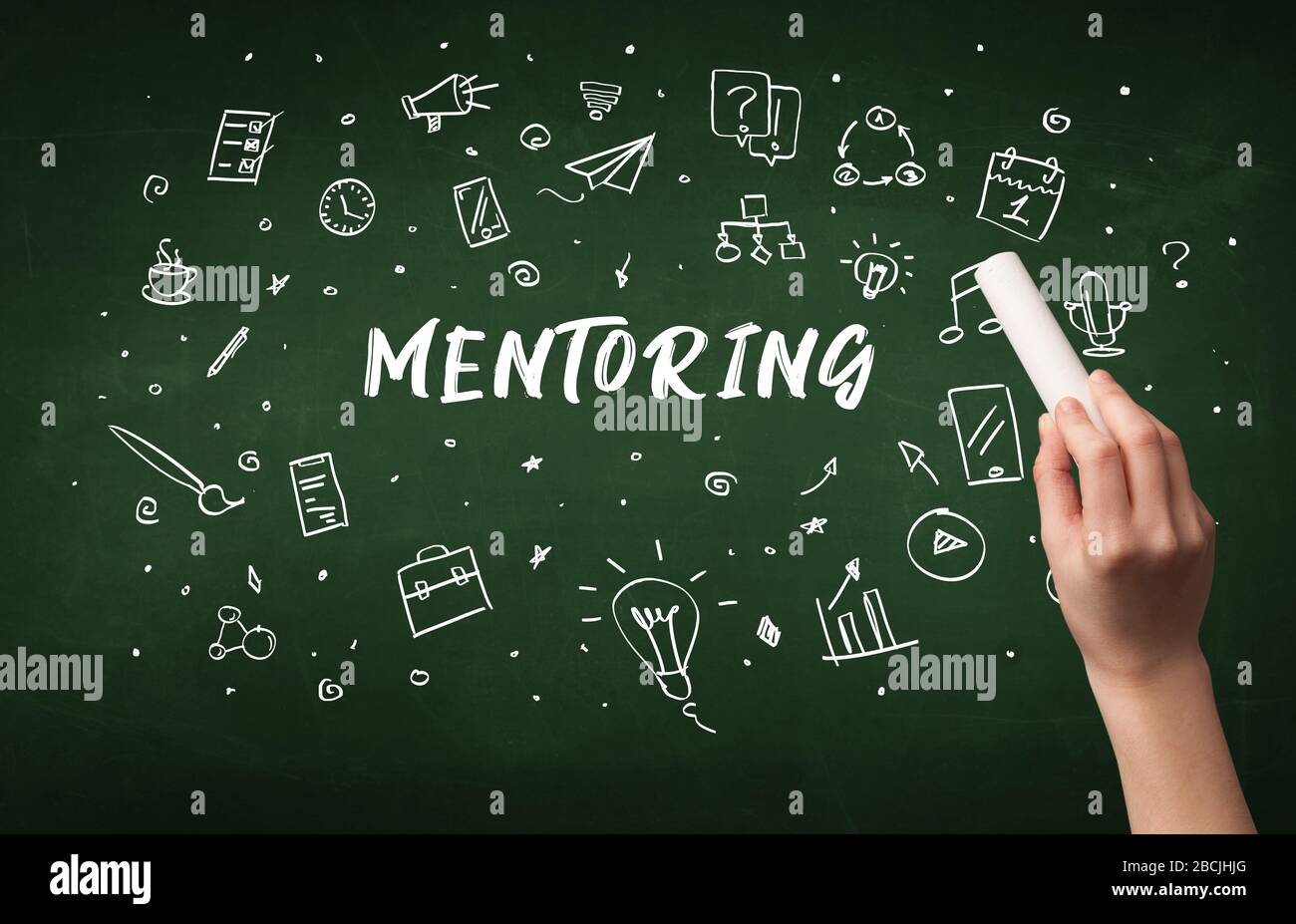 Hand drawing MENTORING inscription with white chalk on blackboard ...