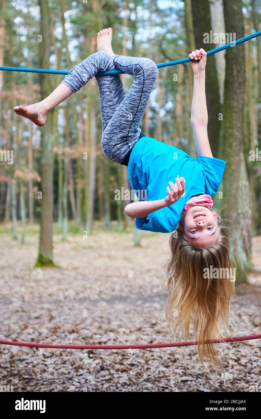 Young child girl hanging on rope upside down on playground in park ...