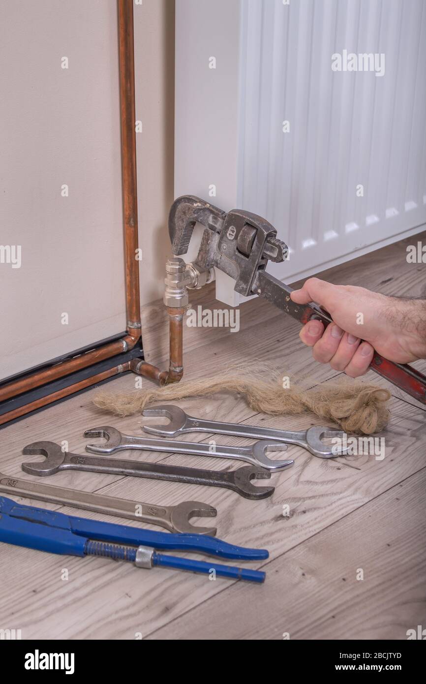 The plumber's hand holds the adjustable wrench and puts it on the valve ...