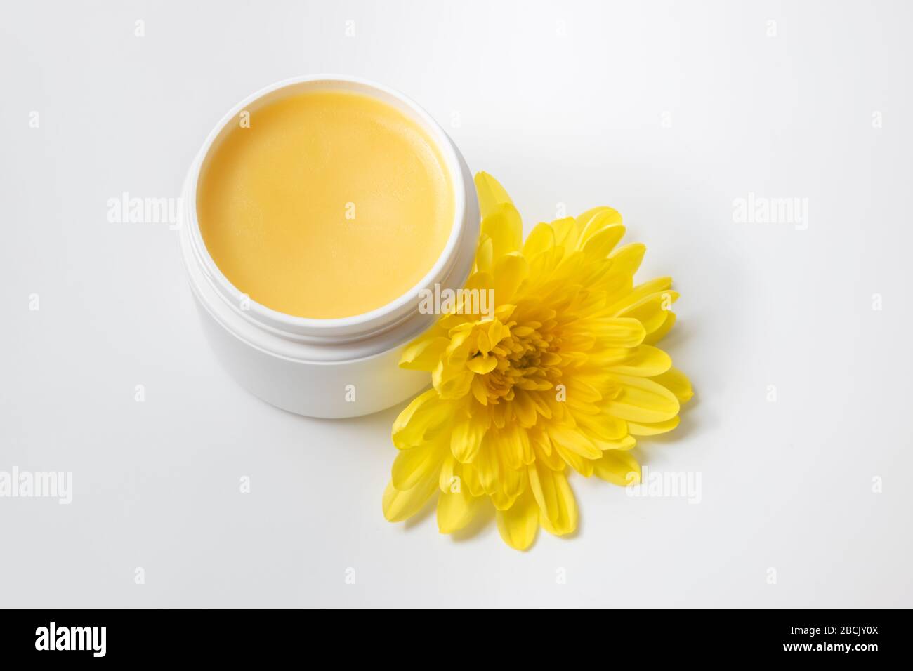 Container of yellow cosmetic cream and flower on white background ...