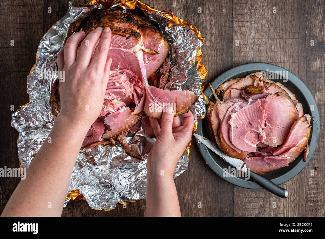 Woman’s hand pulling pieces of ham off a Spiral cut glazed and cooked ...