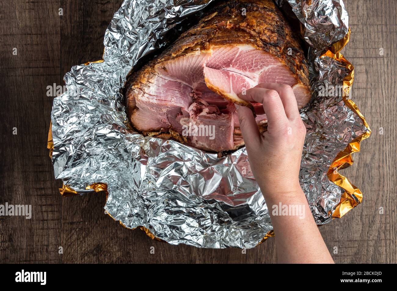 Woman’s hand pulling a piece of ham off a spiral cut glazed and cooked ...