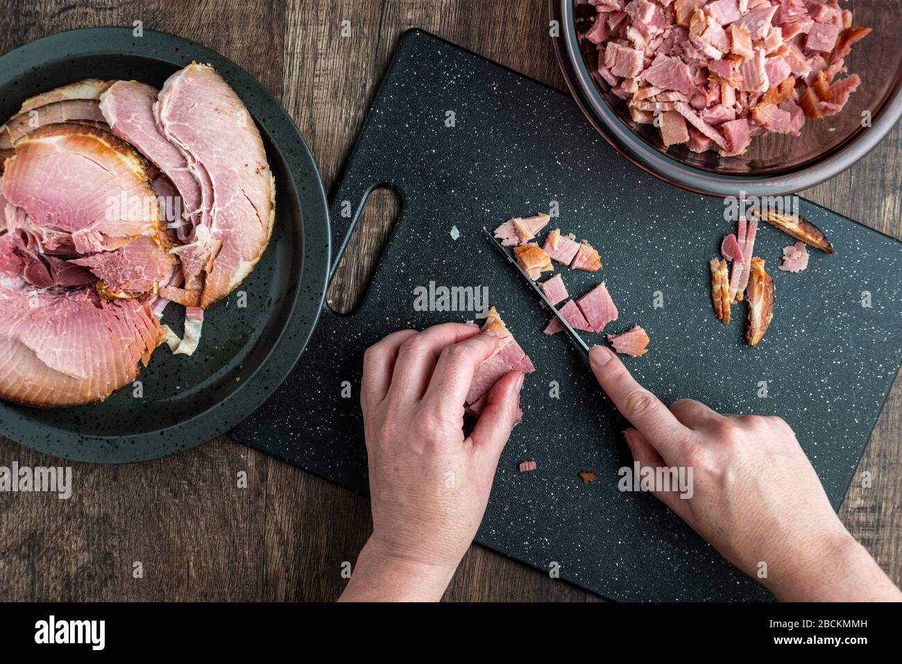 Woman’s hands using knife to slice ham, black plate stacked with ...