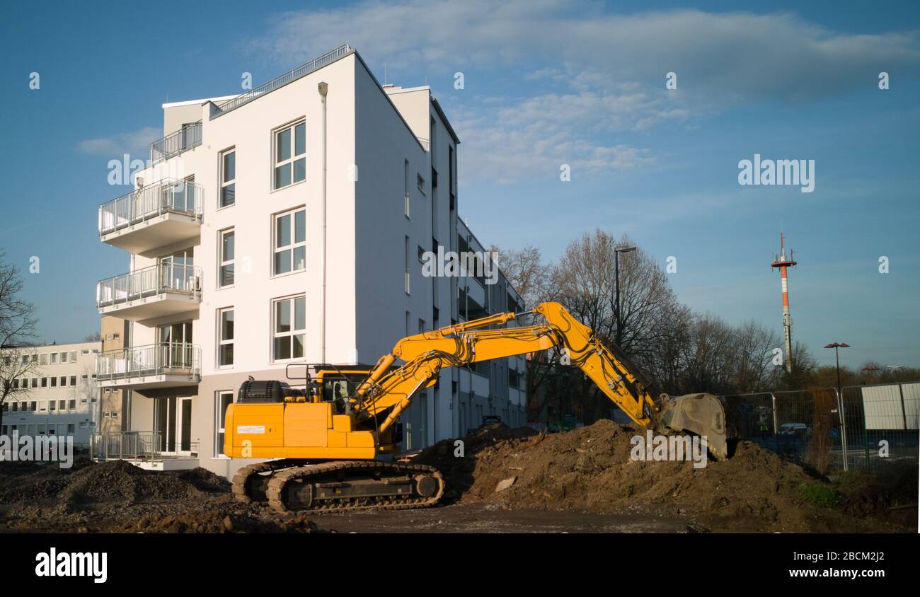 A yellow digger/excavator moving earth in front of a white new building ...
