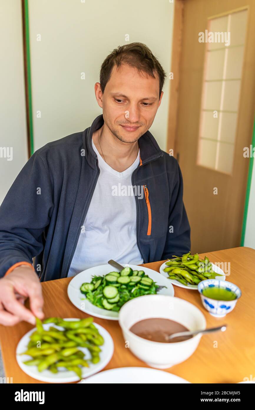 Happy man sitting at table eating green salad dish with Japanese ...