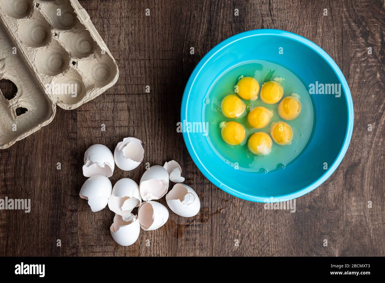 Eight cracked eggs in blue mixing bowl, eggshells, whole eggs in ...