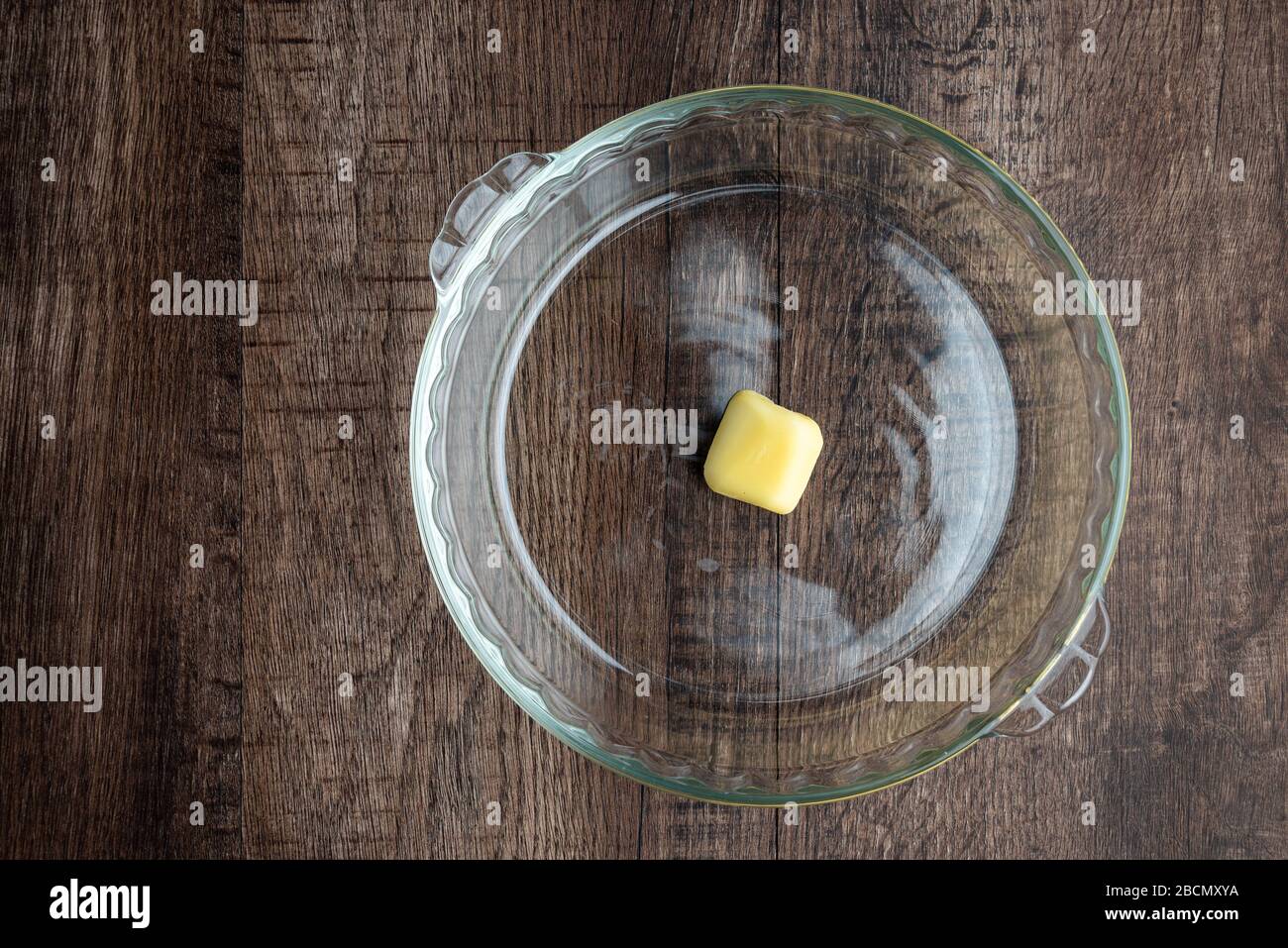 Slab of butter in a glass pie pan, ready to butter dish, wood table ...
