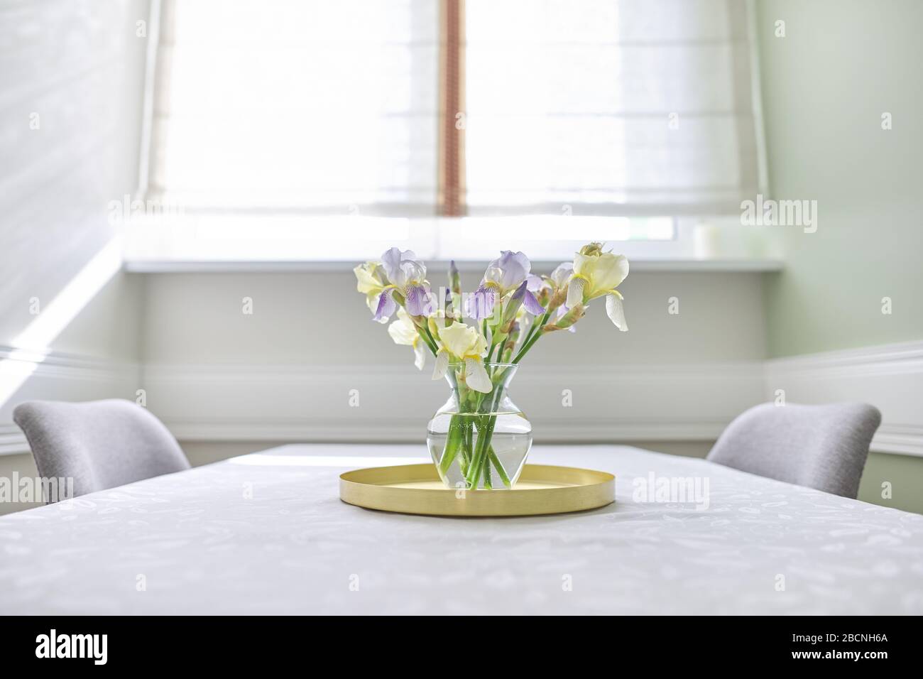Vase with bouquet of yellow and purple irises on table near the window ...