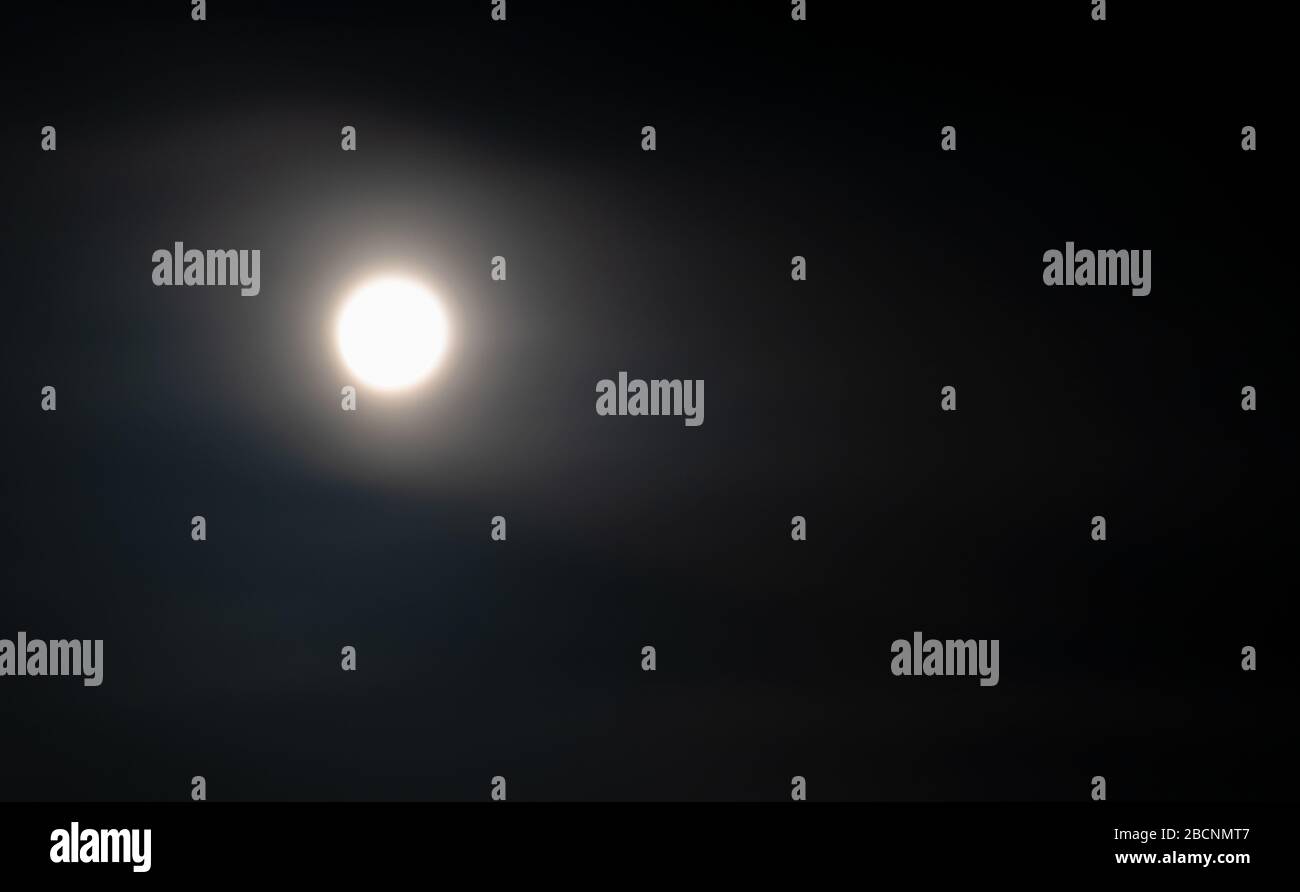 The moon on the night sky in a haze of clouds. The full moon ...