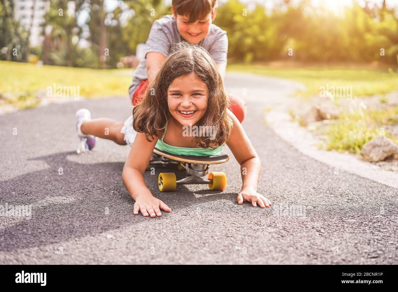 Happy brother and sister playing with longboard outdoor - Young people ...