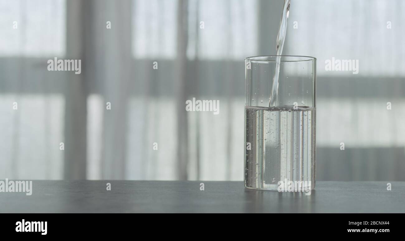 pour water into glass on concrete countertop with window on background ...