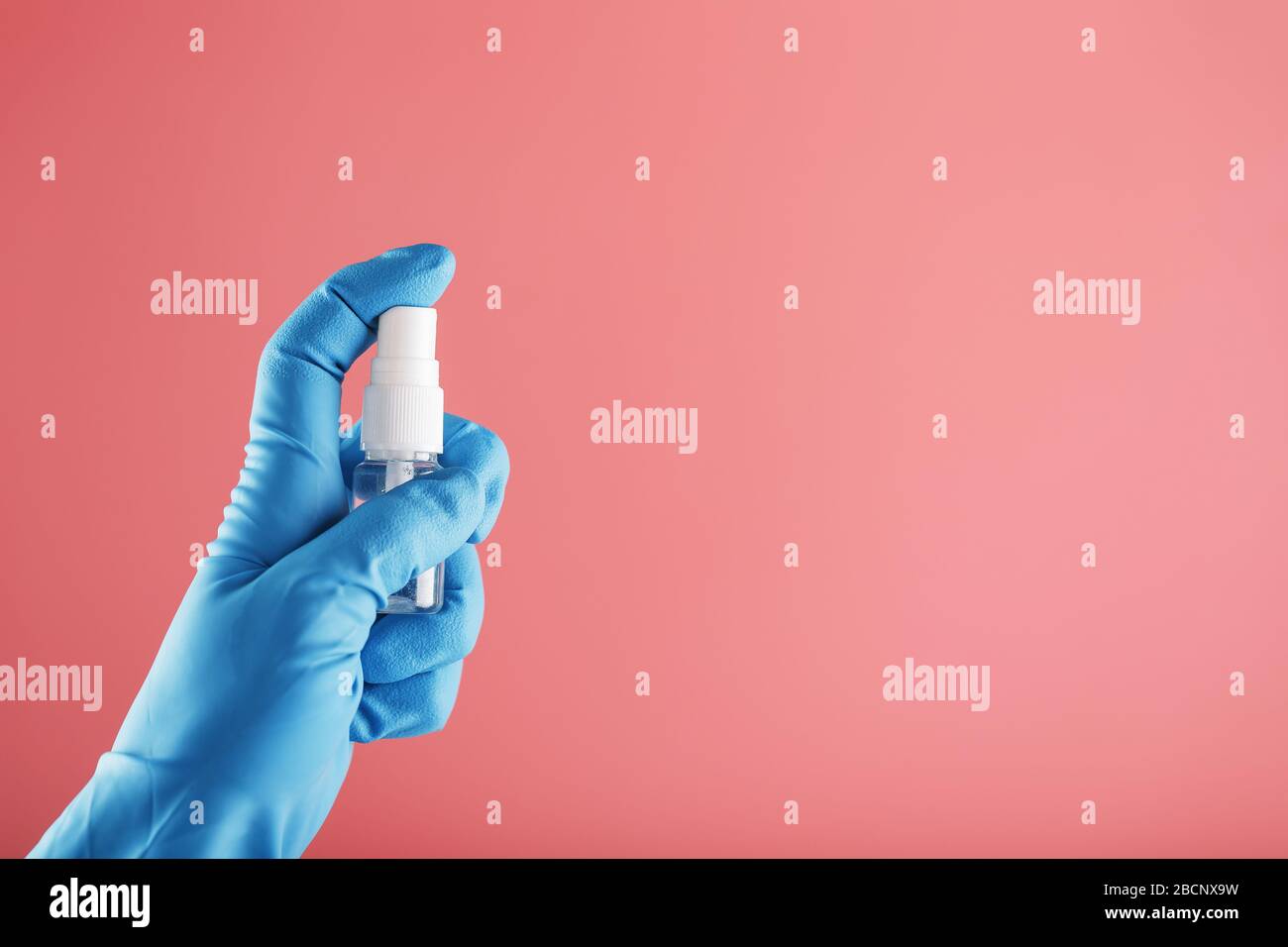 A blue-gloved hand holds a disinfectant on a pink background ...