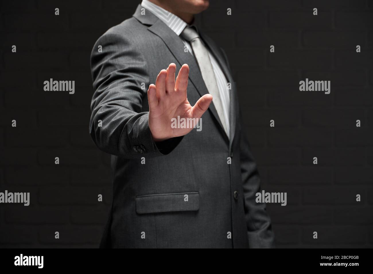 businessman portrait showing palm of hand, dressed in gray suit, dark ...