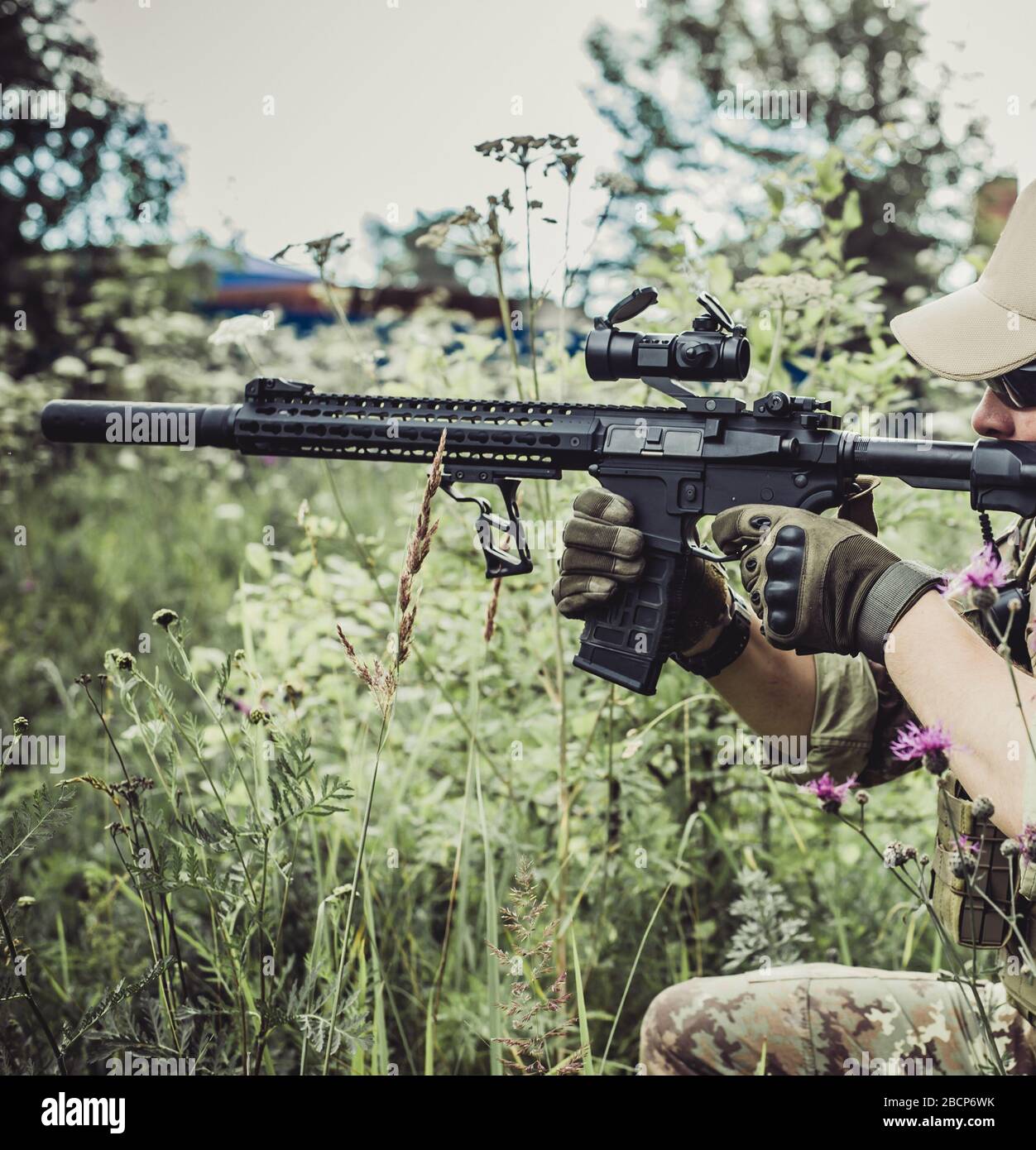 A military man or airsoft player in a camouflage suit sits in the grass ...