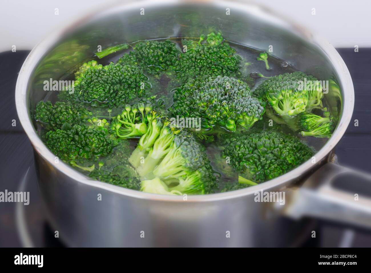 Cooking organic broccoli florets in a small stainless steel pan in a ...